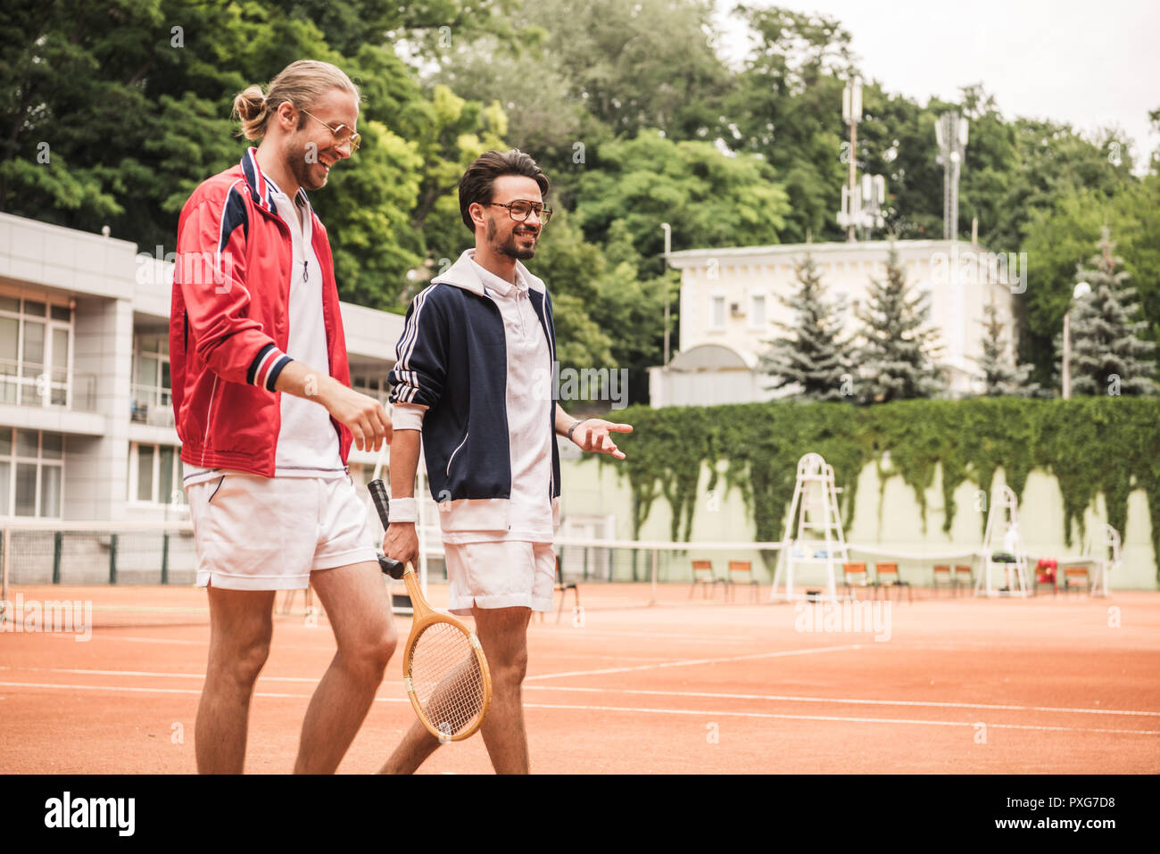smiling friends with wooden rackets walking on tennis court Stock Photo ...