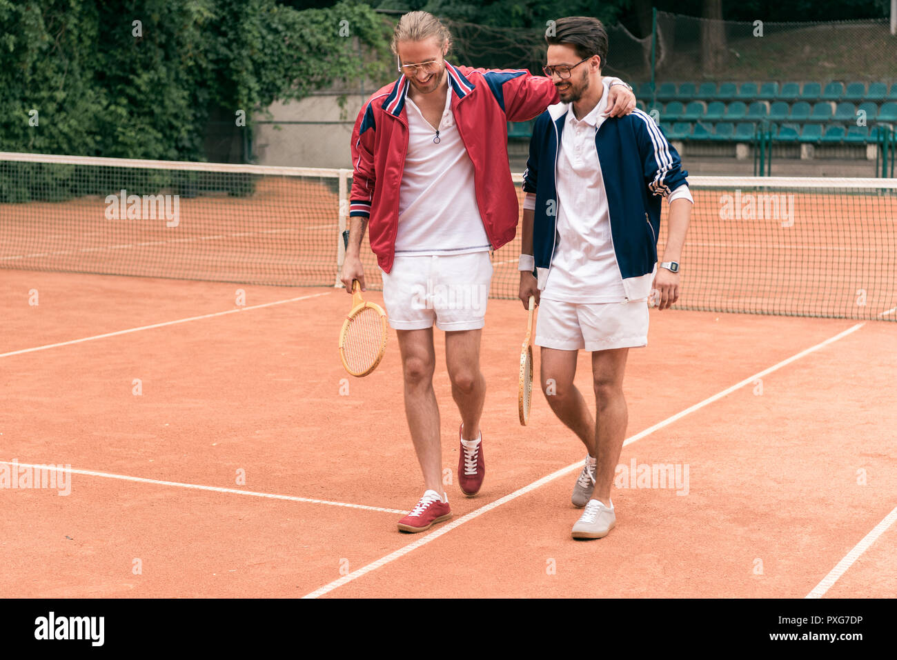 cheerful sportive friends with wooden rackets hugging and walking on ...