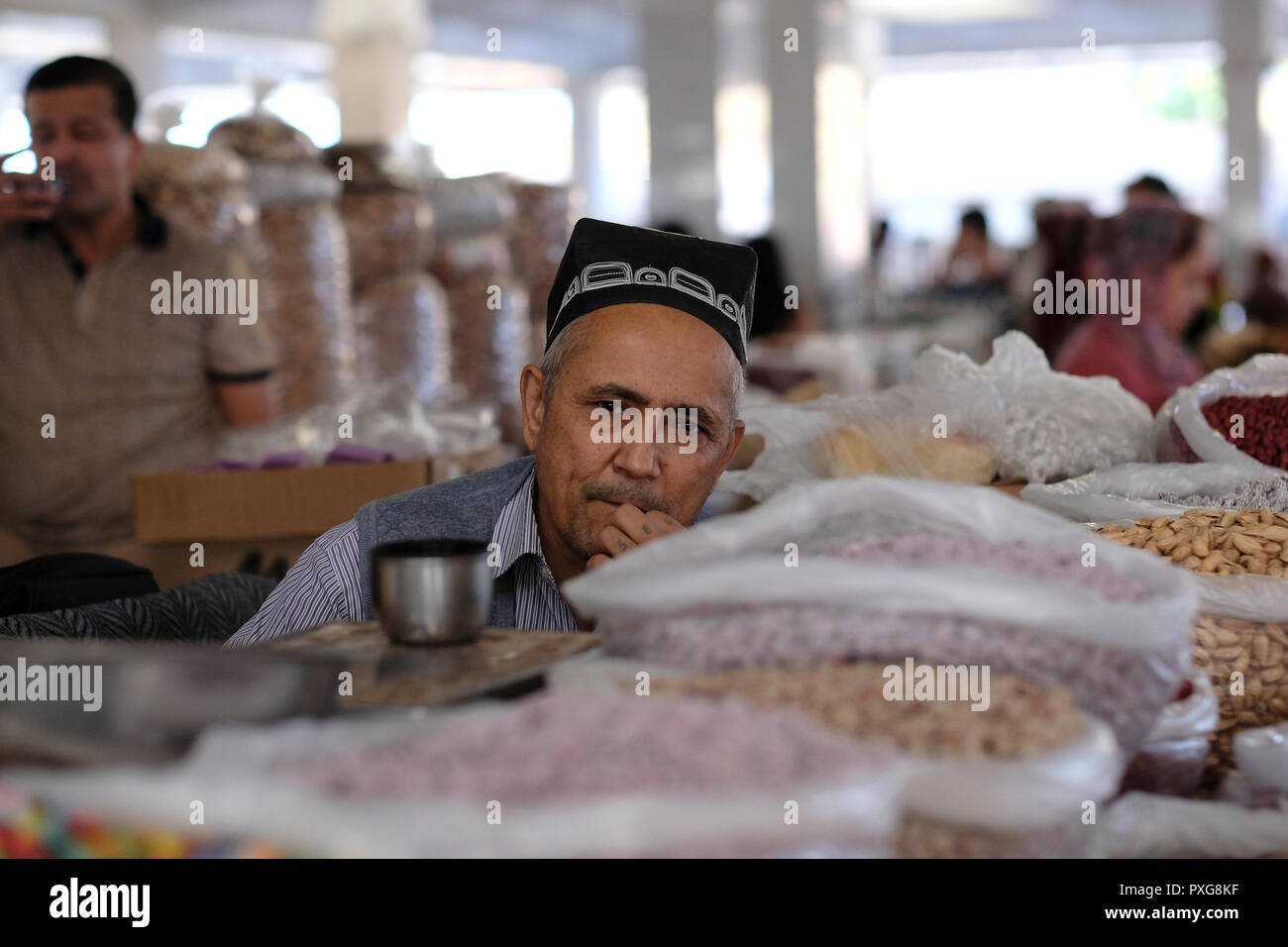 A vendor wearing traditional Uzbek doppa or duppi cap selling dried ...
