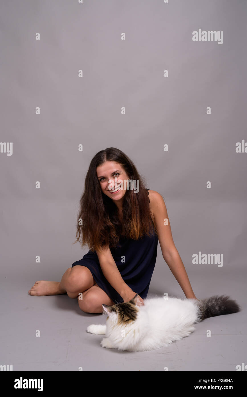 Portrait of young beautiful woman with cat against gray background ...