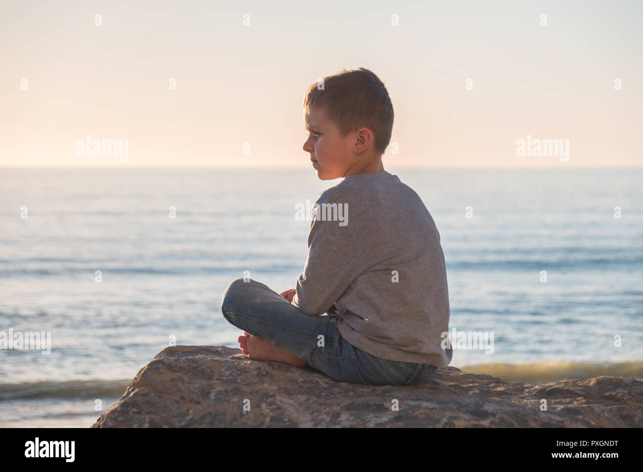Lonely barefoot boy sitting on the rock at Glenelg beach and thinking ...
