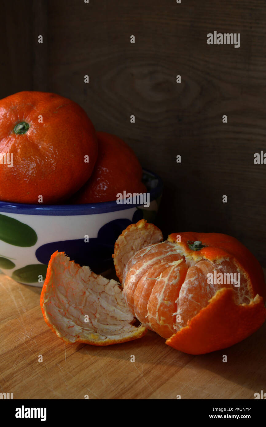 Bright orange clementines in blue and white bowl and a partially peeled ...