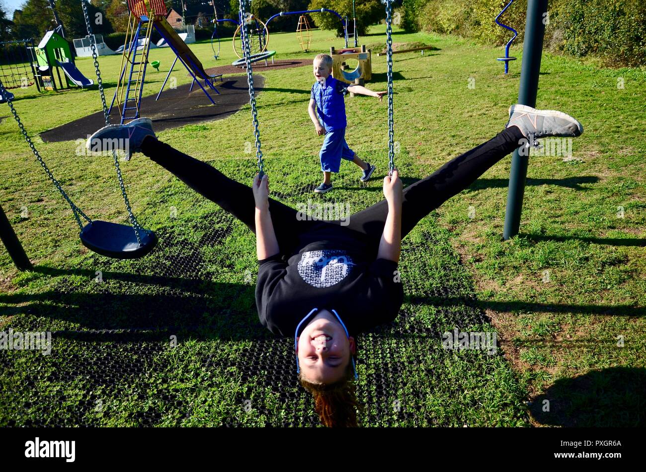 Young girl hanging upside down on playground swing with young boy ...