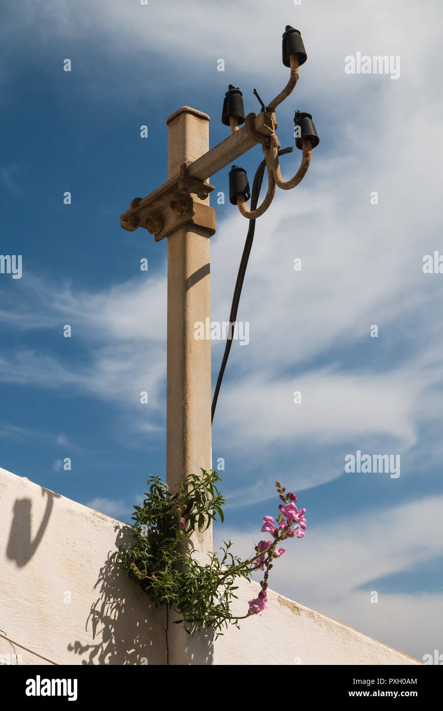 Side of a building with a roof line. Electricity column with one cable ...