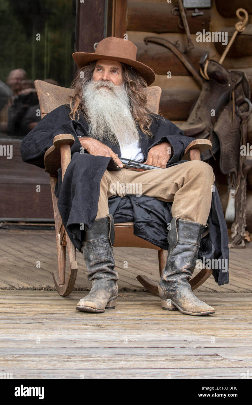 Western man in traditional clothing with a colt 45 sitting on a log ...