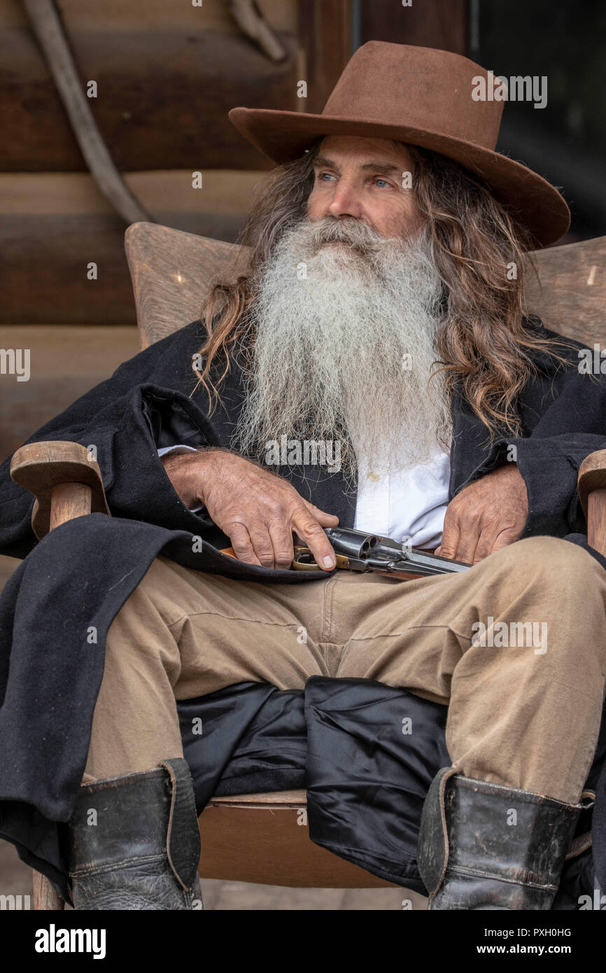 Western man in traditional clothing with a colt 45 sitting on a log ...