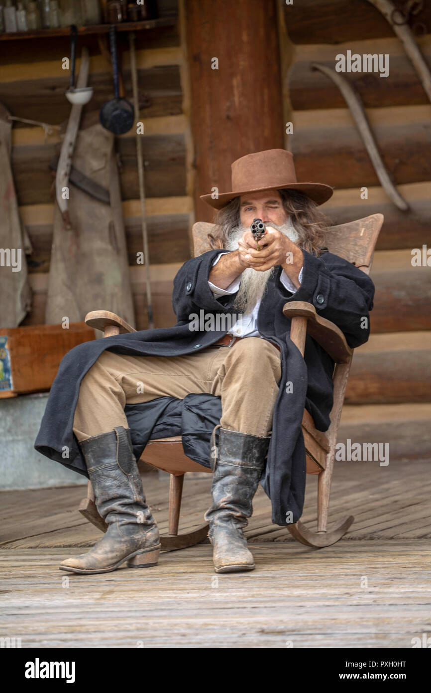 Western man in traditional clothing with a colt 45 sitting on a log ...