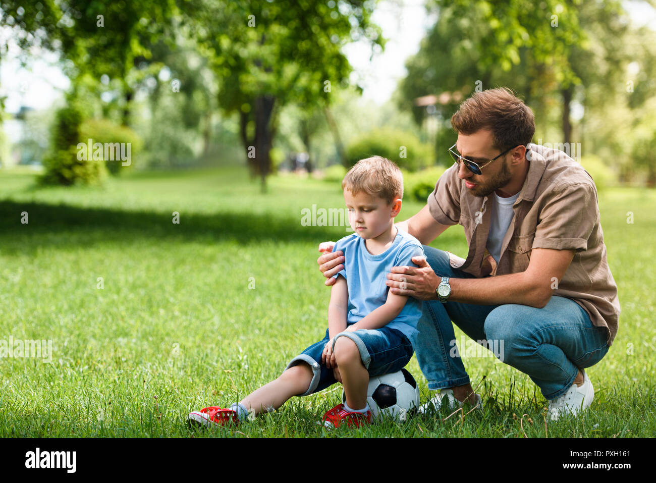 father hugging and supporting sad son after playing football at park ...