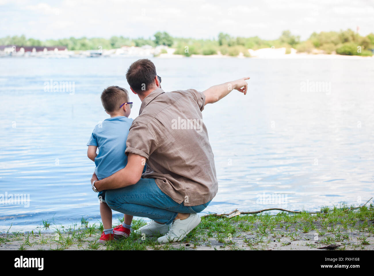 back view of father pointing on something at river to son at park Stock ...