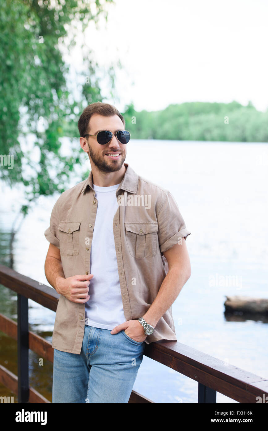 smiling handsome man leaning on railing near lake at park Stock Photo ...