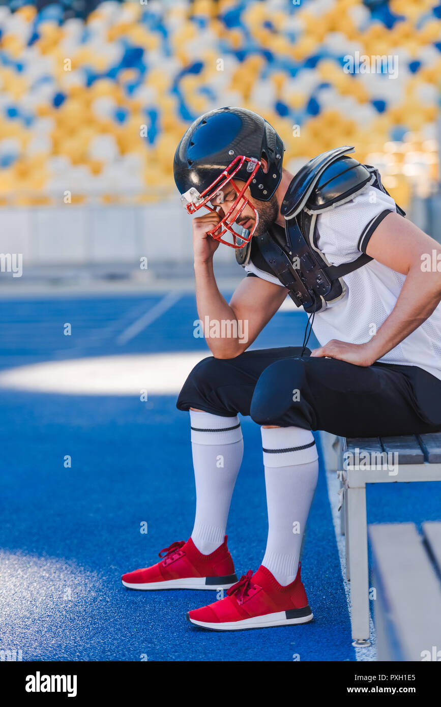 depressed young american football player sitting at sports stadium ...