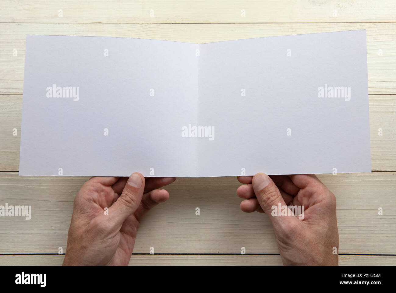 Mens hands holding empty white booklet on wooden background. View from ...