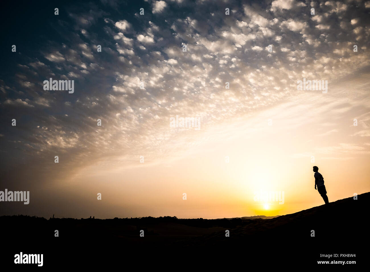 Man in black silhouette standing on the ground during a warm yellow ...
