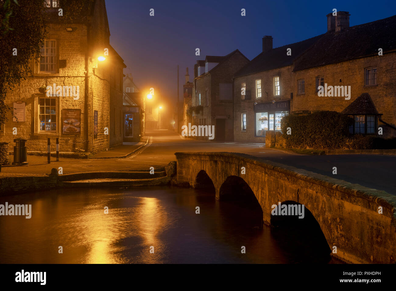 Mist and fog at dawn in the cotswold village of Bourton on the Water in ...