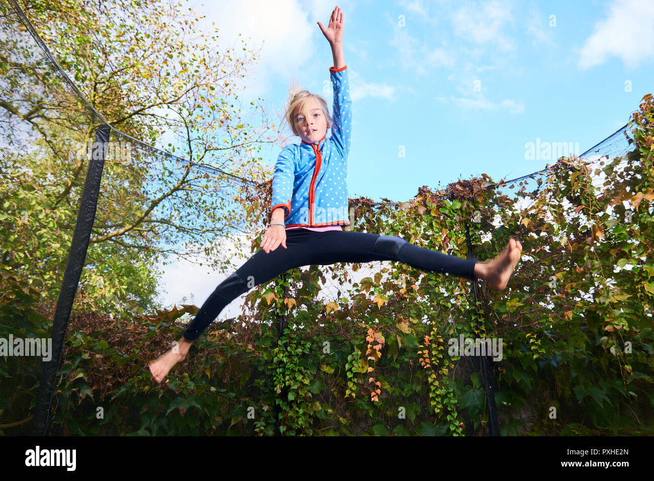 Child cute blond girl playing and jumping on trampoline with greenery ...