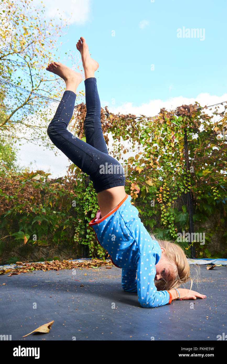Child cute blond girl playing and jumping on trampoline with greenery ...