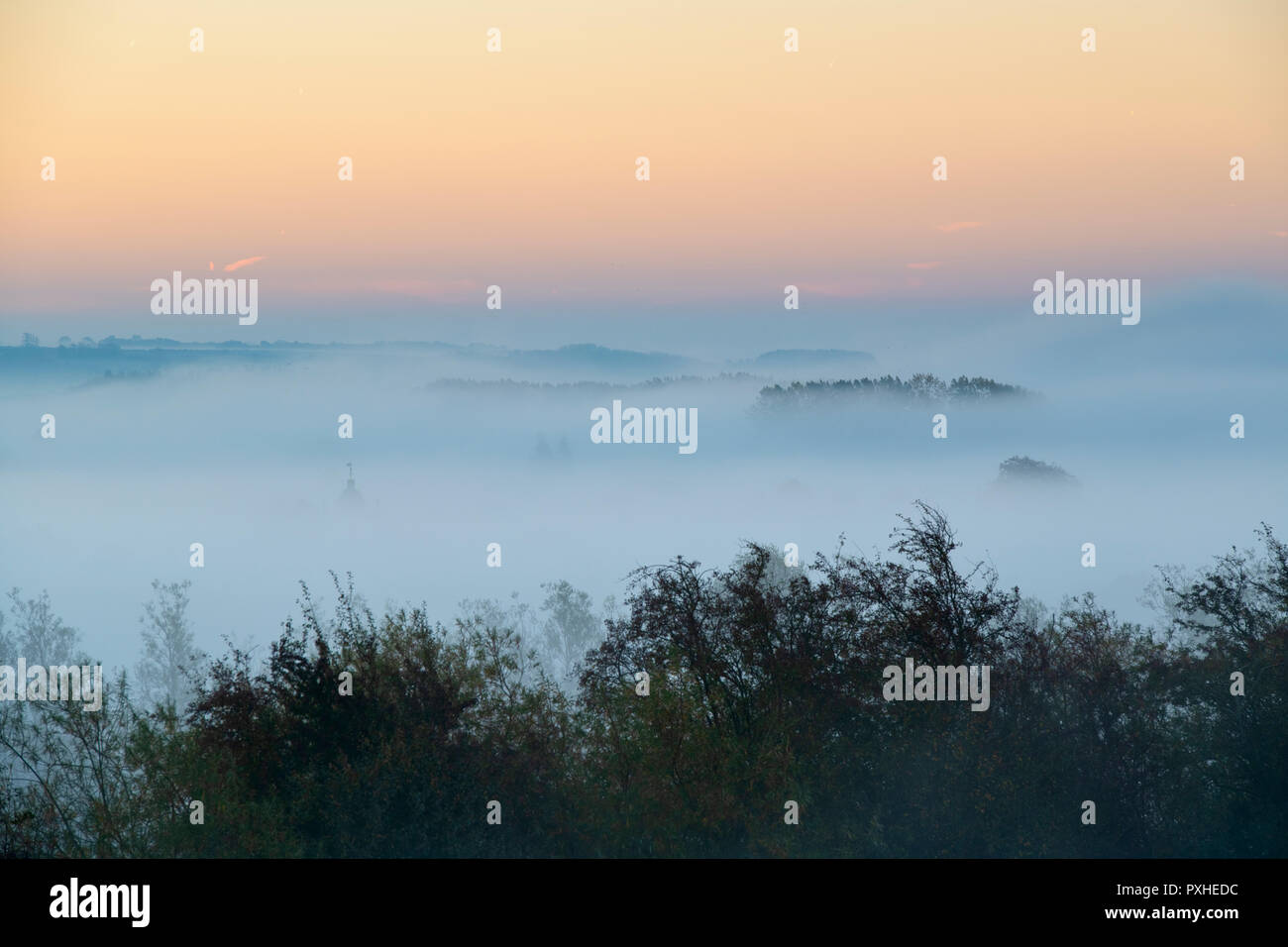 Mist and fog at sunrise rolling over the cotswold village of Bourton on ...
