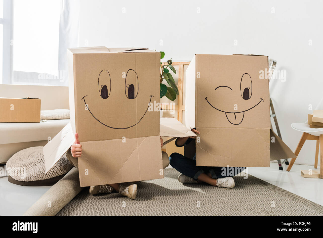 obscured view of couple with cardboard boxes on heads sitting on floor ...