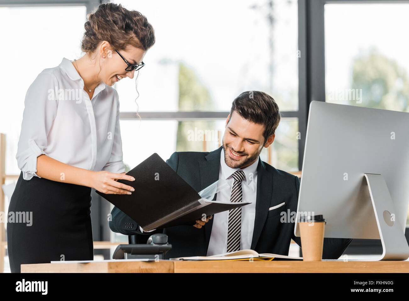 smiling secretary showing folder with documents to handsome businessman ...