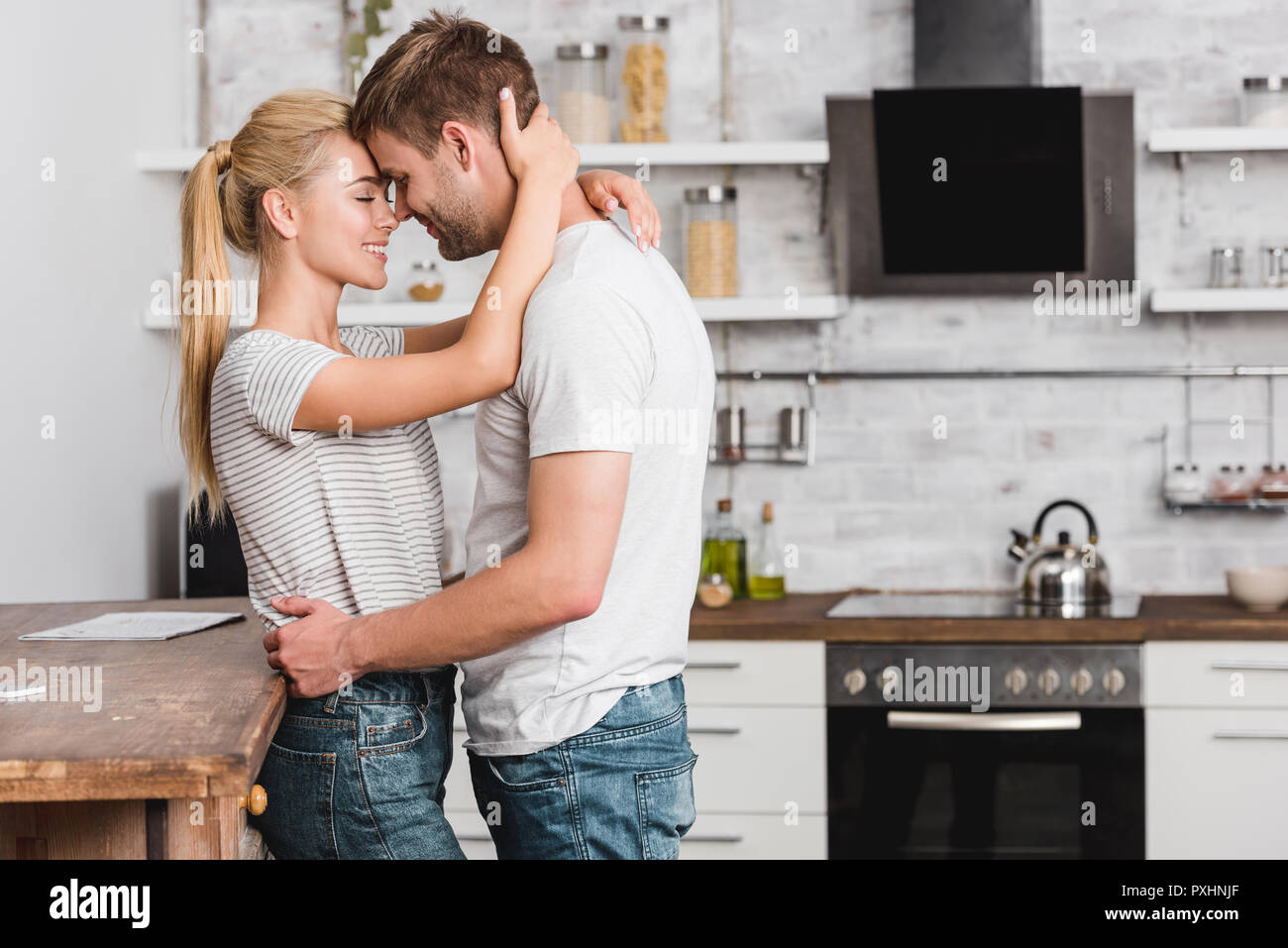 side view of couple cuddling in kitchen and leaning on kitchen counter ...