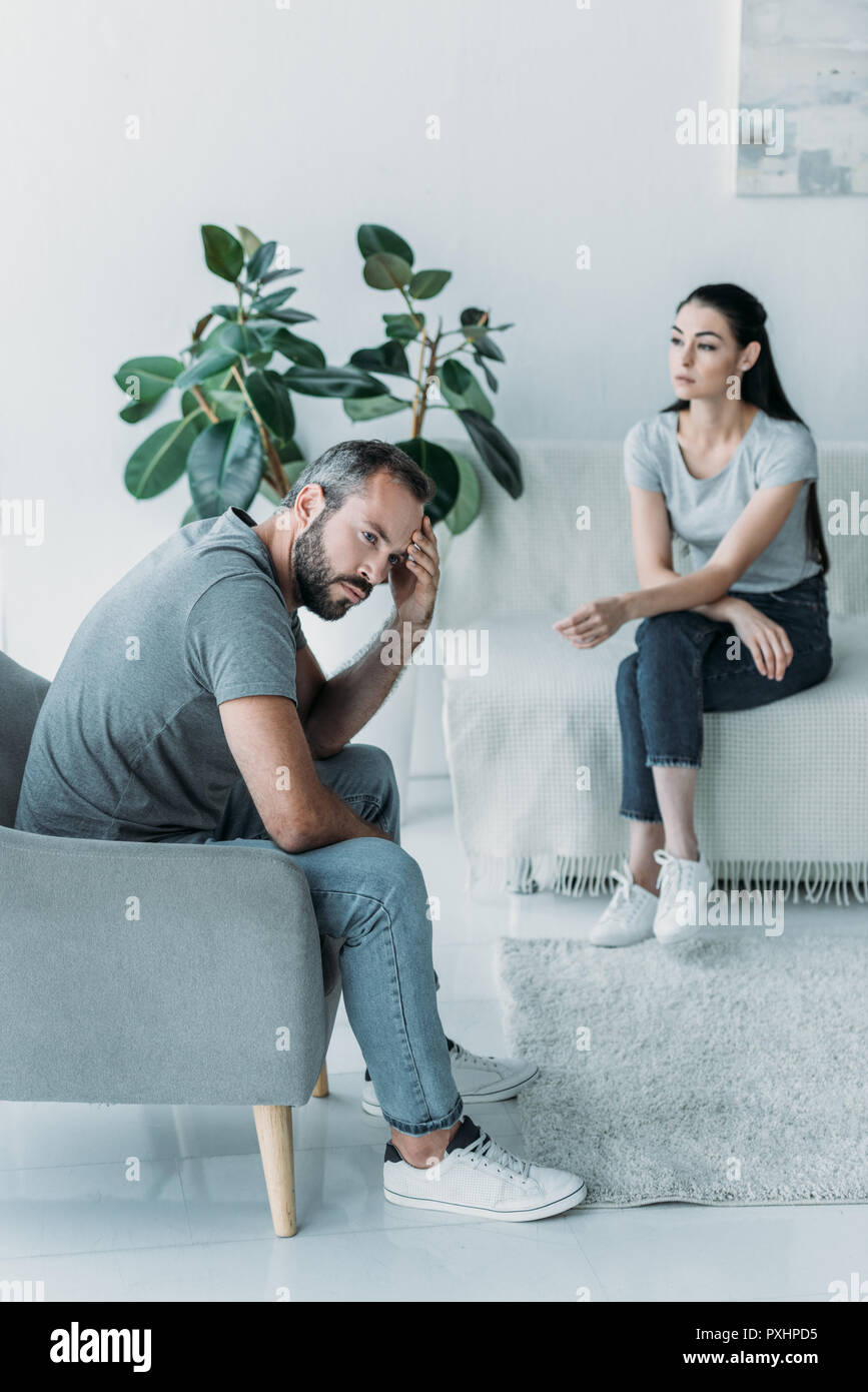 high angle view of frustrated partners sitting on armchair and couch ...