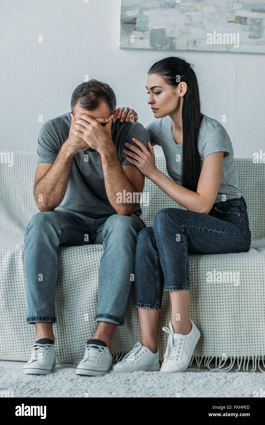 young woman supporting sad boyfriend sitting on couch with hands on ...