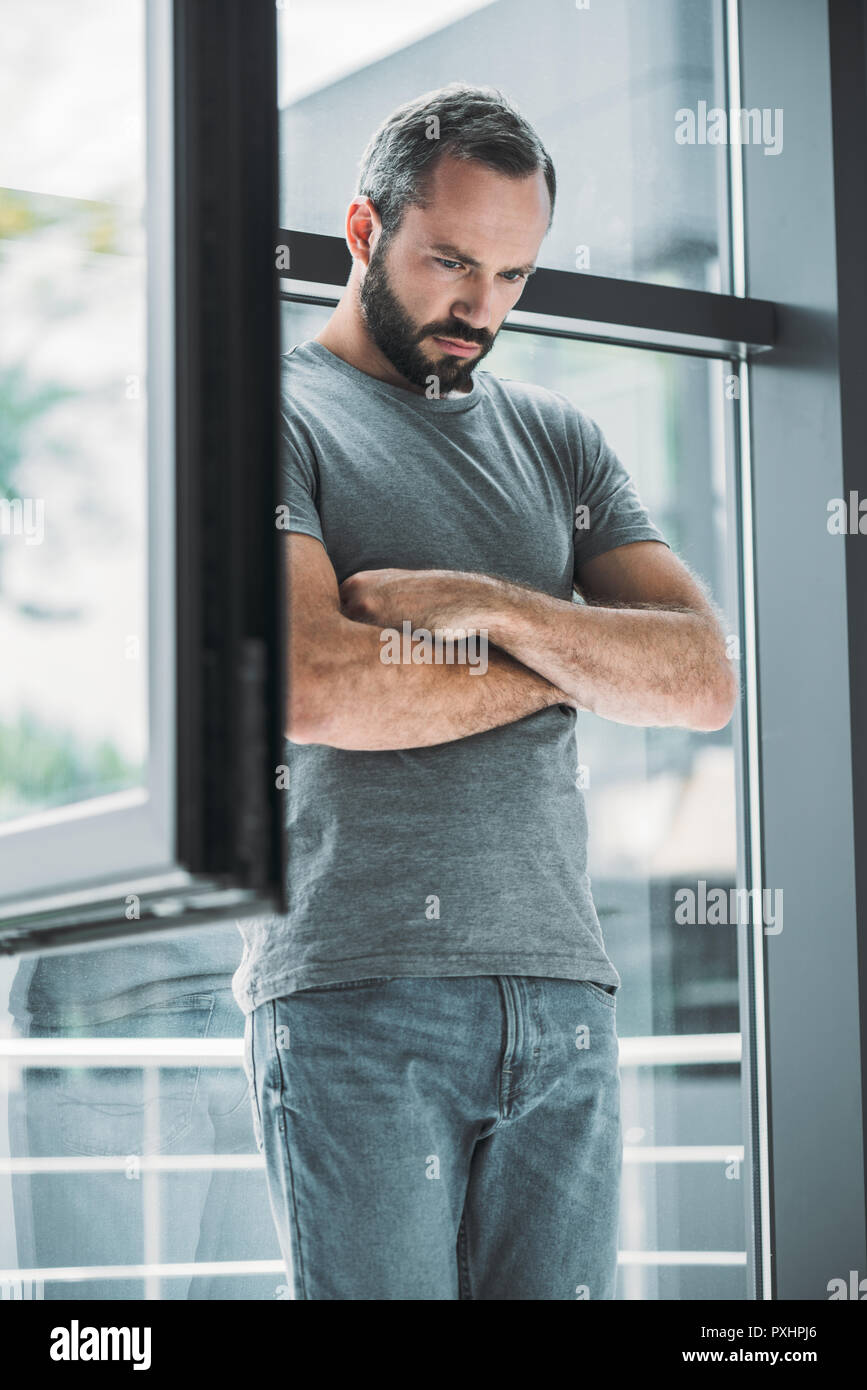 upset middle aged bearded man standing with crossed arms and looking ...