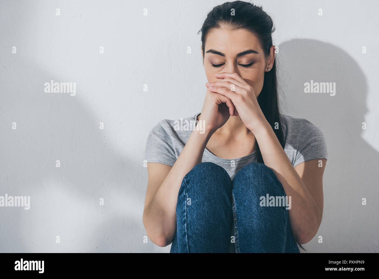 sad stressed girl sitting with closed eyes near grey wall Stock Photo ...