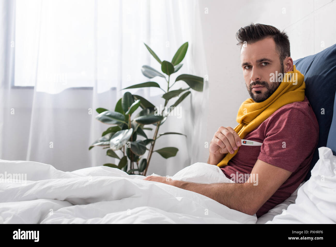 diseased young man measuring temperature with electronic thermometer in ...