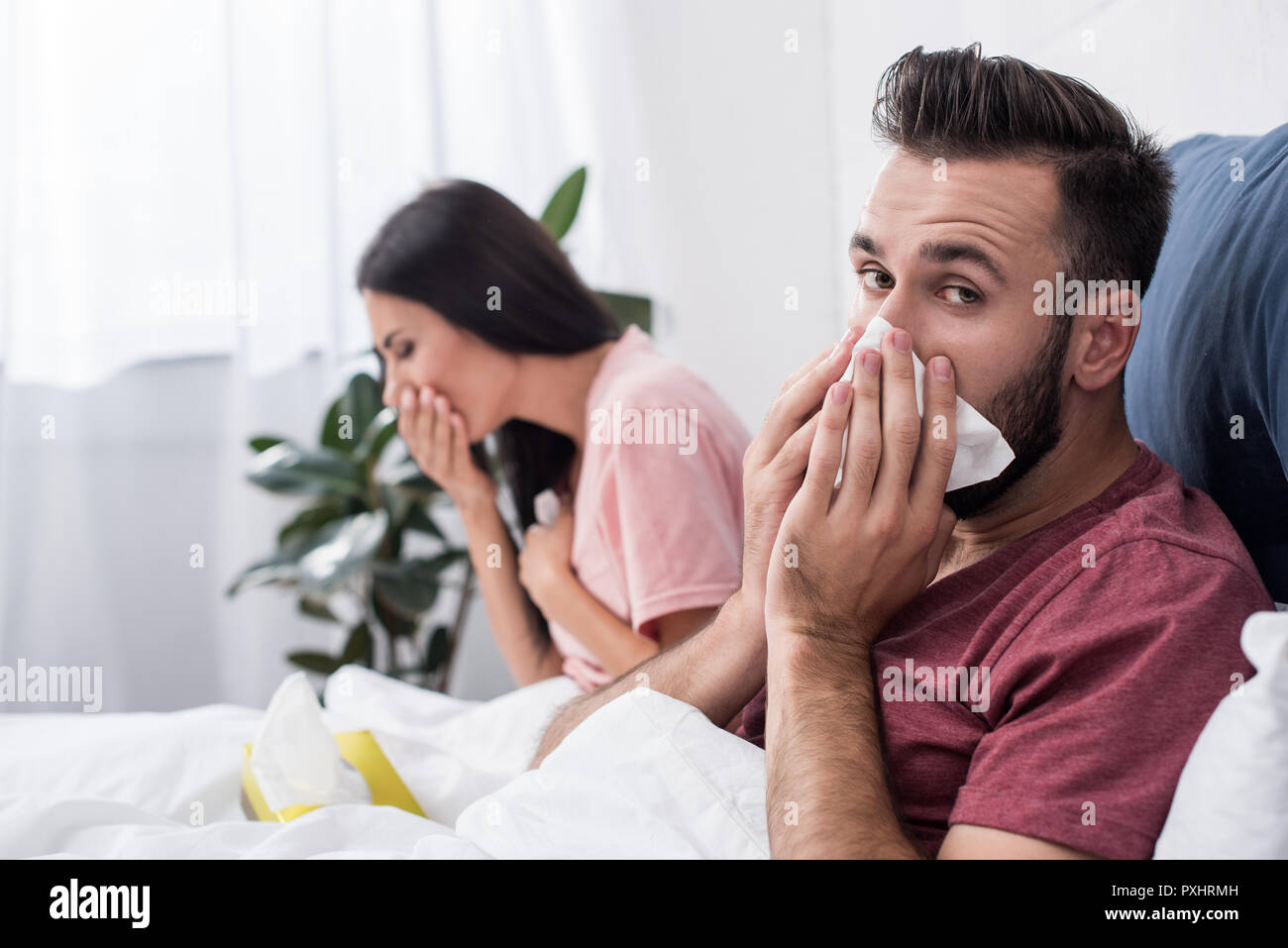 diseased young sick couple sneezing into paper napkins while sitting in ...