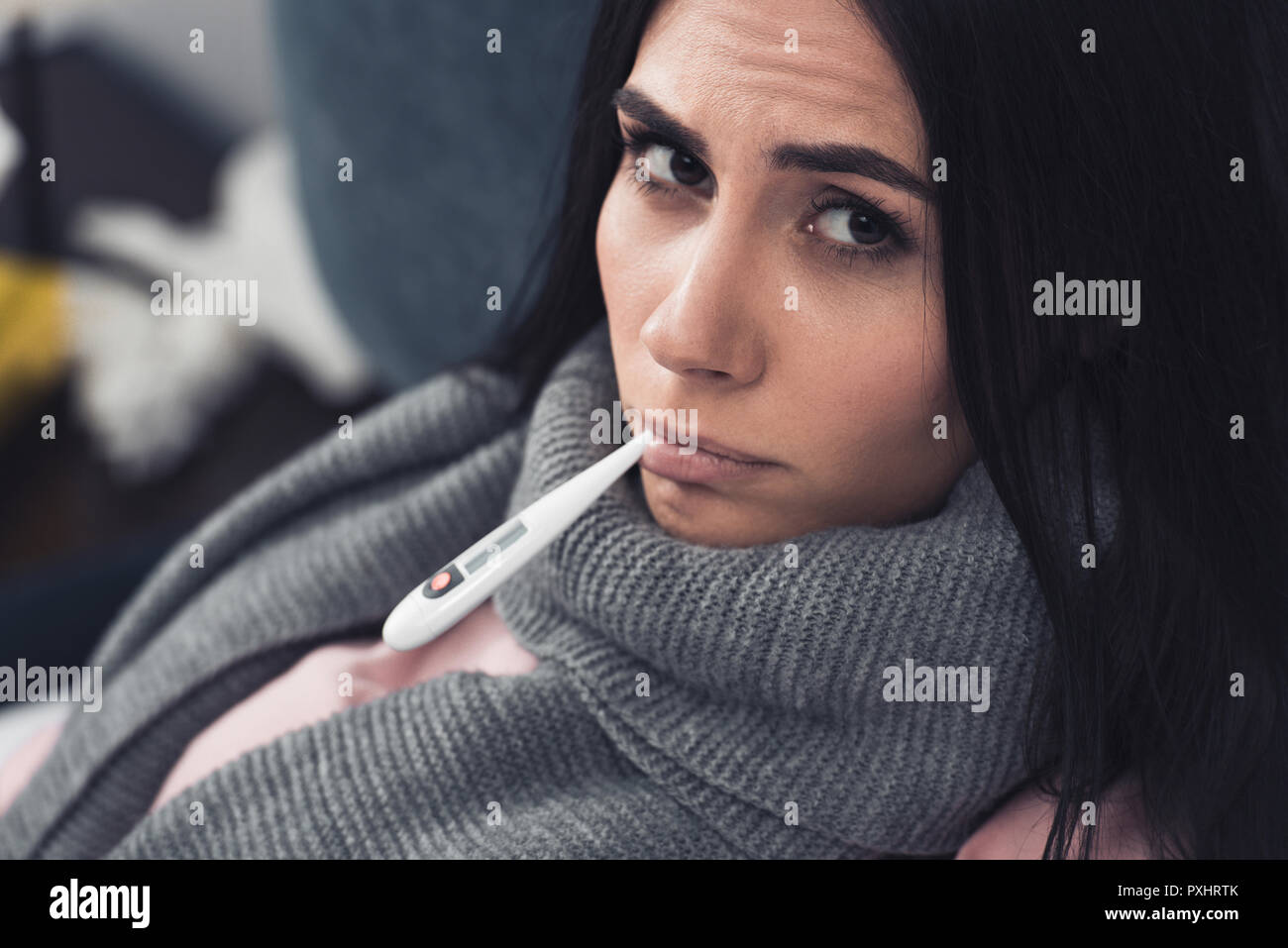 sick young woman measuring temperature with mouth thermometer and ...