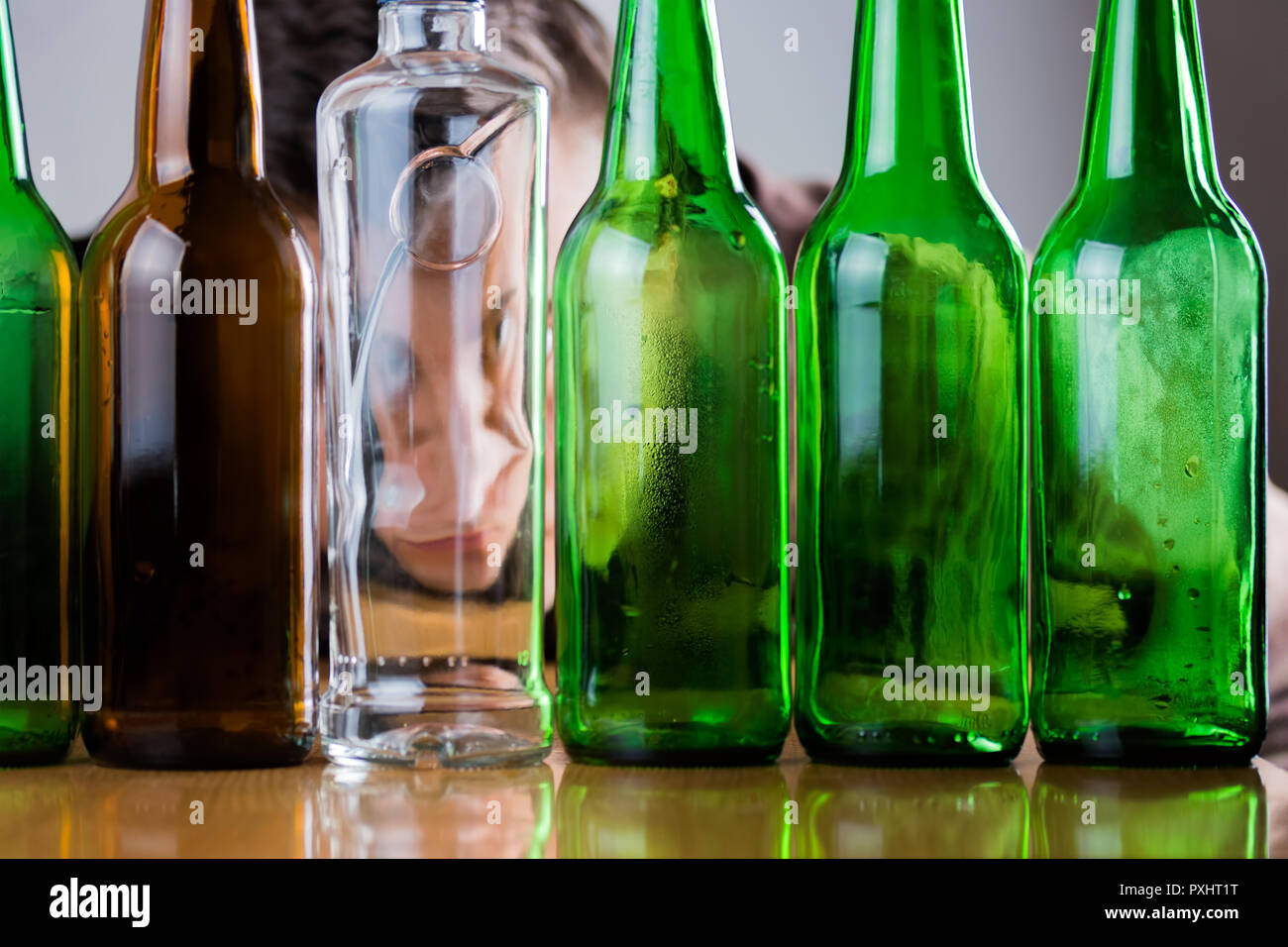 Sad young man behind green and brown glass bottles. Fighting alcohol ...