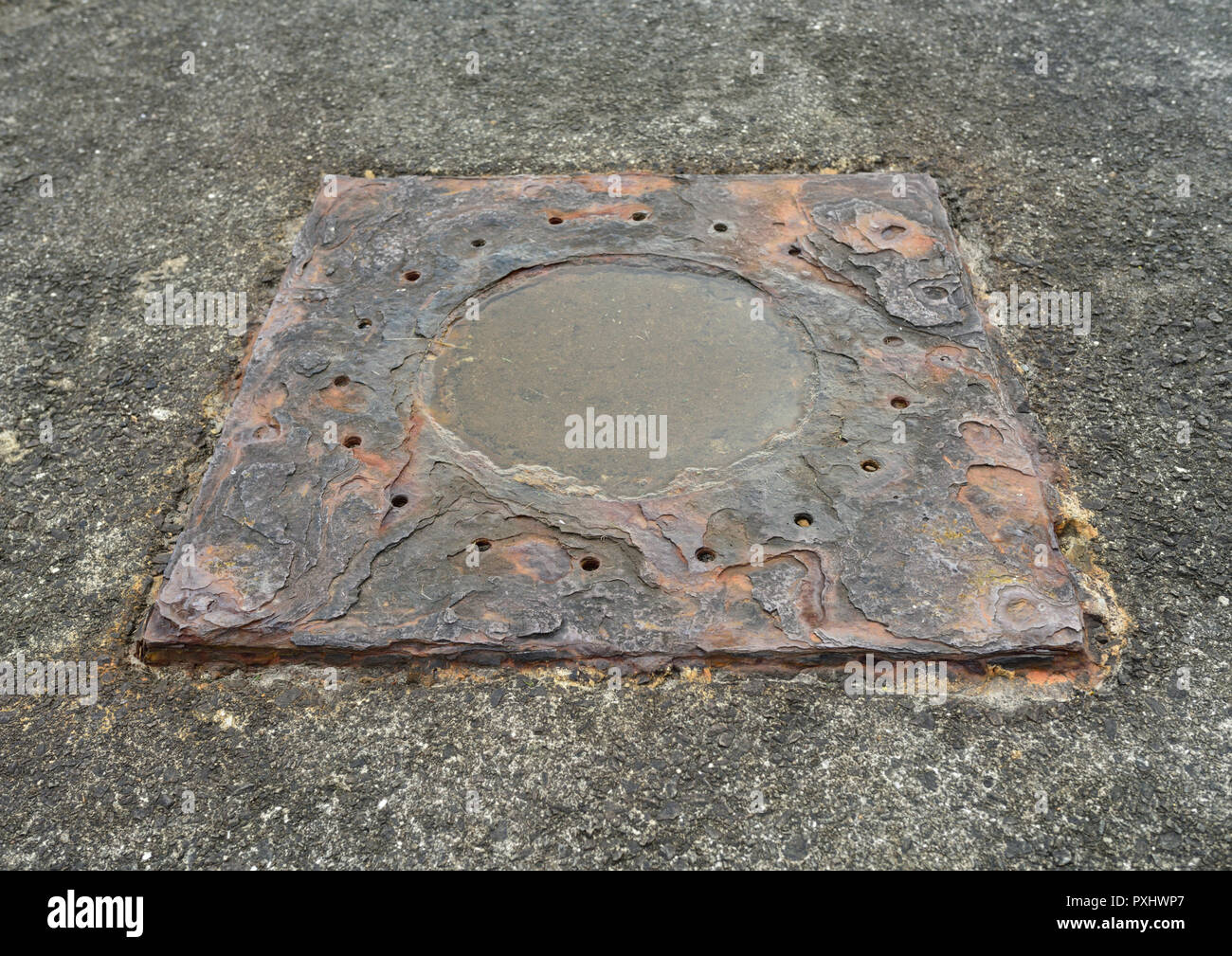 Rusty steel plate with water lying in shallow hole in the centre, set ...