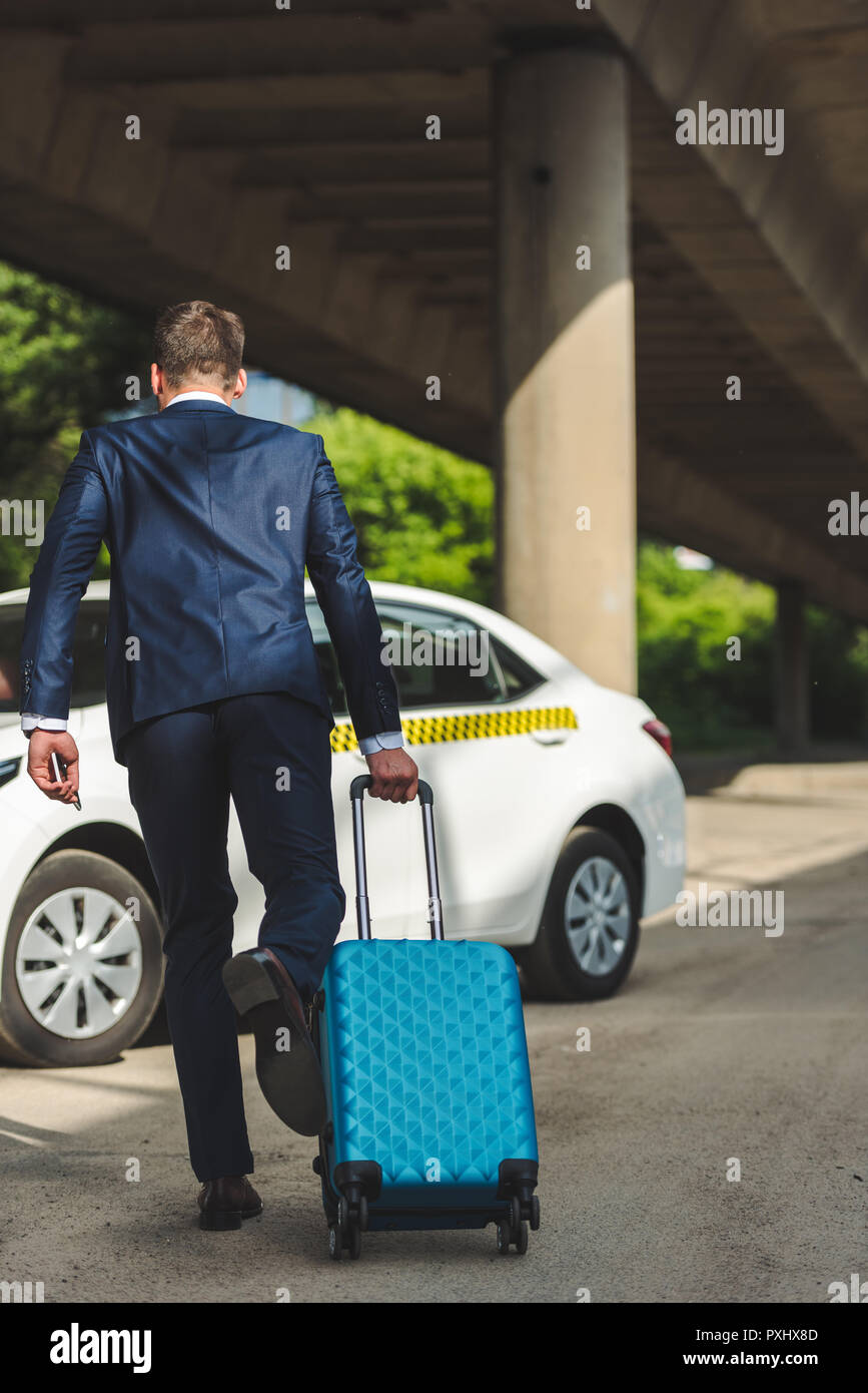 back view of stylish young man with suitcase running to taxi Stock ...