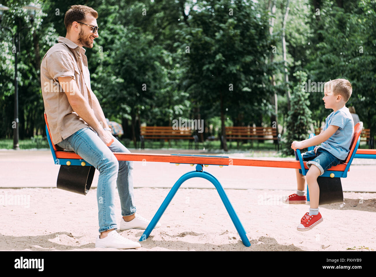 side view of father and son having fun on swing at playground in park ...