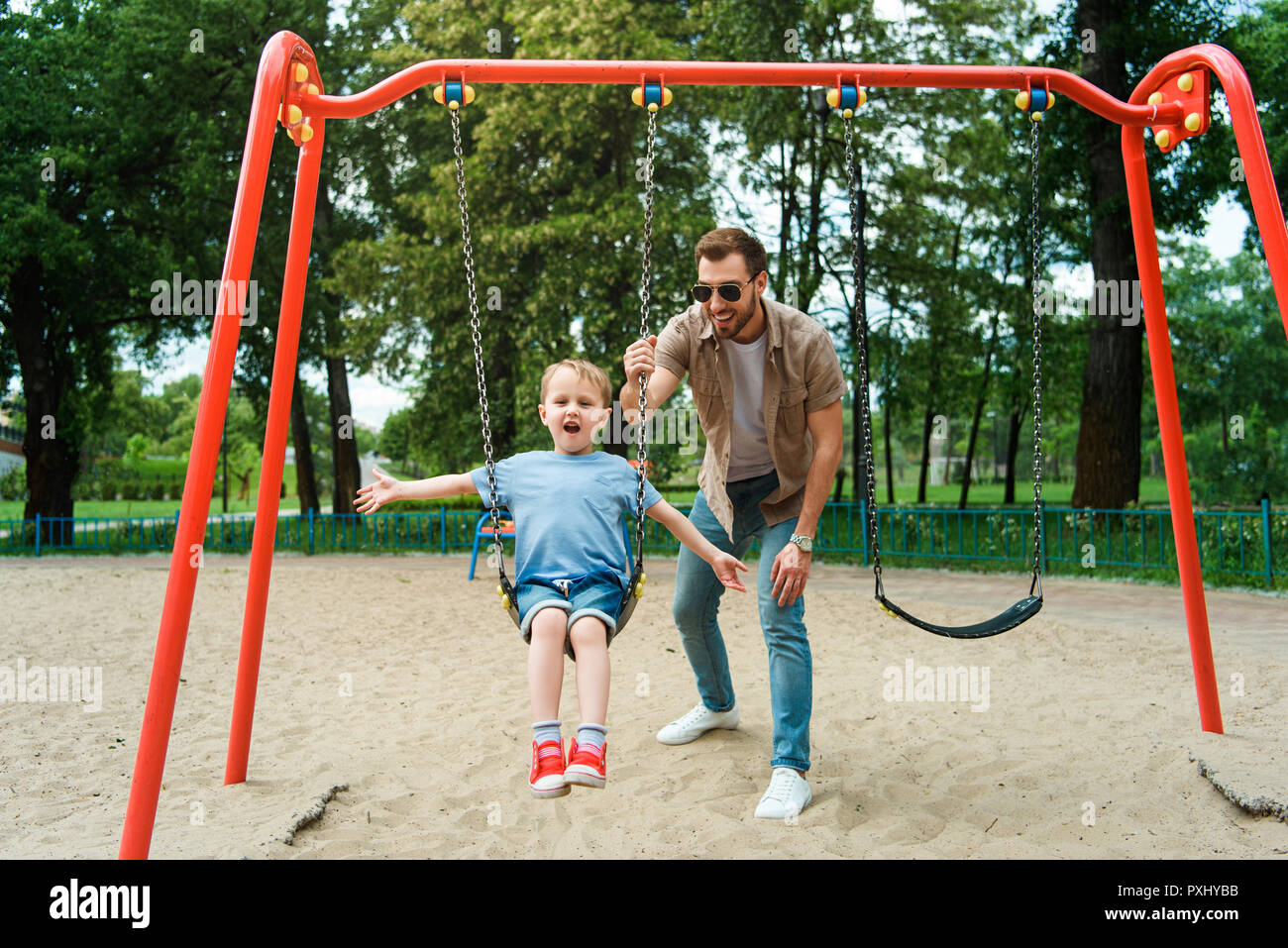 father and son having fun on swing at playground in park Stock Photo ...