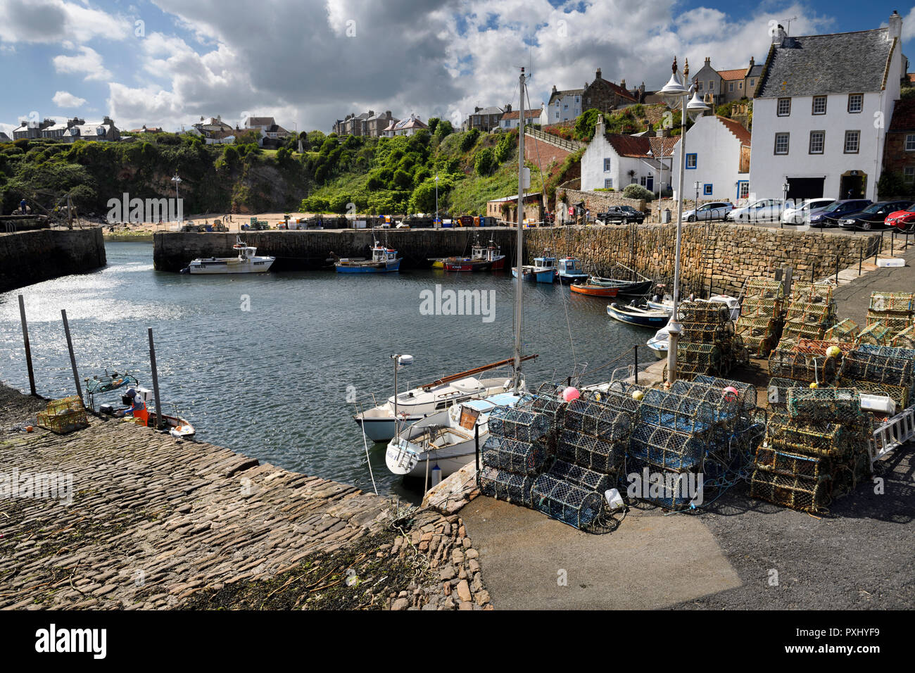 Stone pier walls at Crail Harbour with fishing boats and lobster traps ...