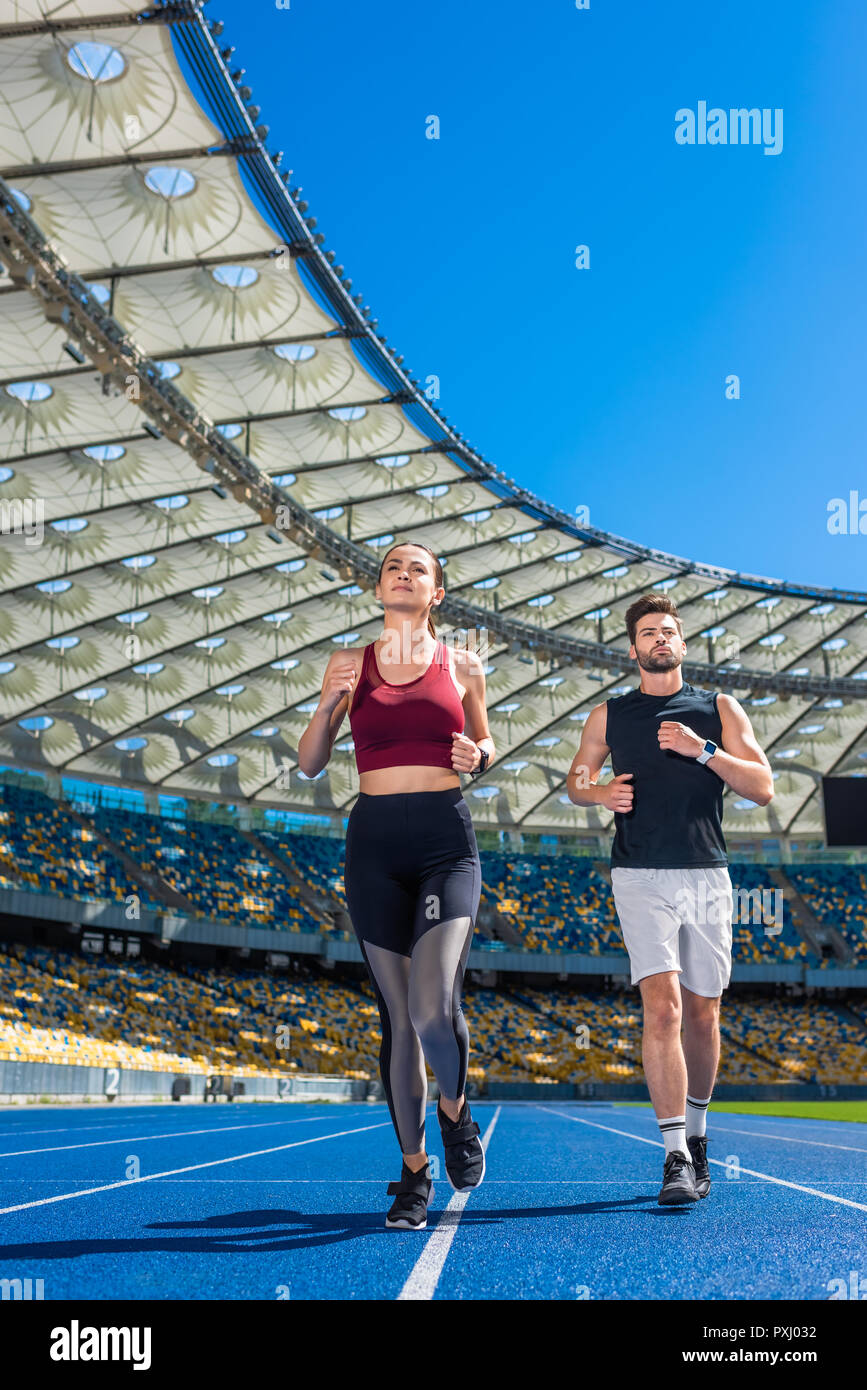 fit young male and female joggers running on track at sports stadium ...