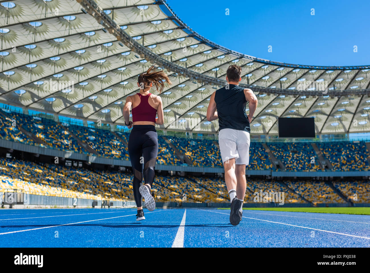 rear view of male and female joggers running on track at sports stadium ...