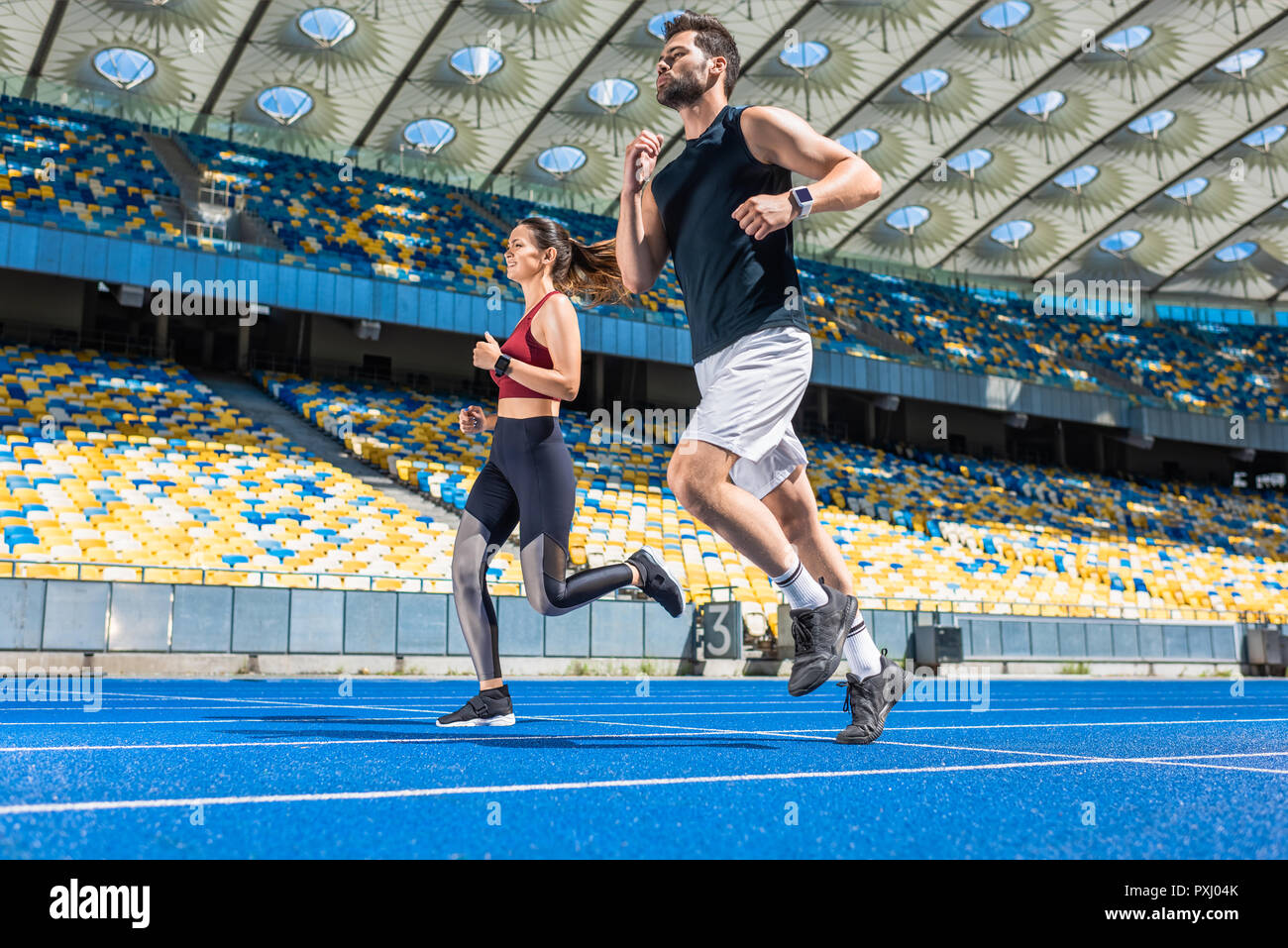 motion shot of young male and female joggers running on track at sports ...