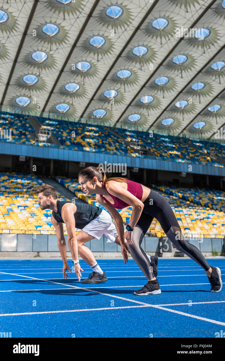 fit young male and female sprinters in start position on running track ...