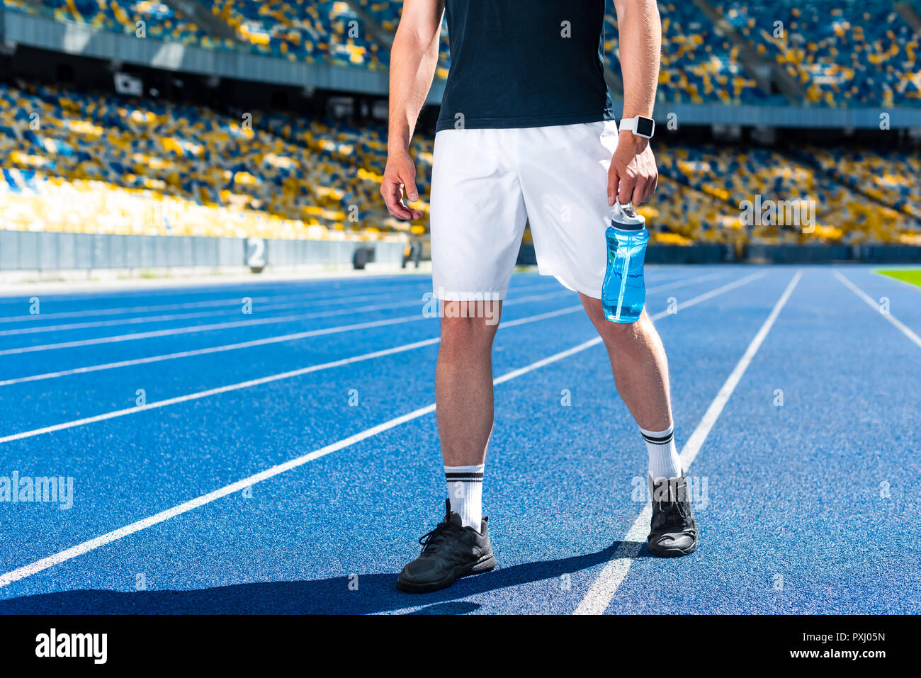 cropped shot of sportsman with fitness water bottle at sports stadium ...