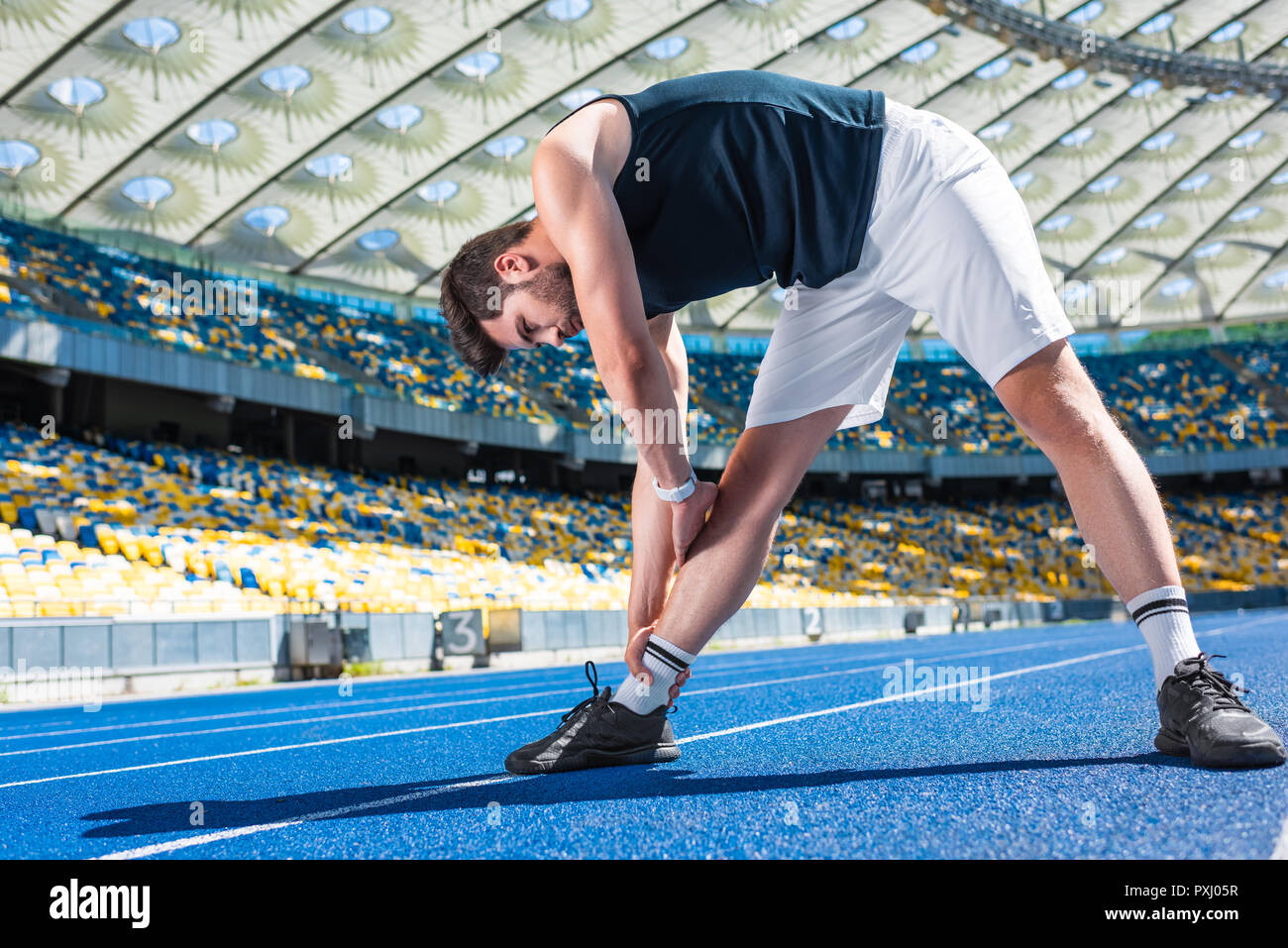 handsome young man stretching on running track at sports stadium Stock ...