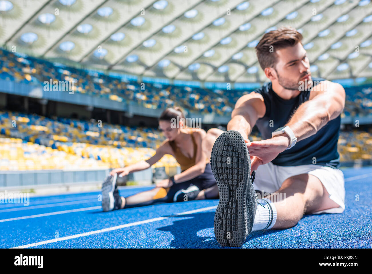 young athletic couple sitting on running track and stretching at sports ...