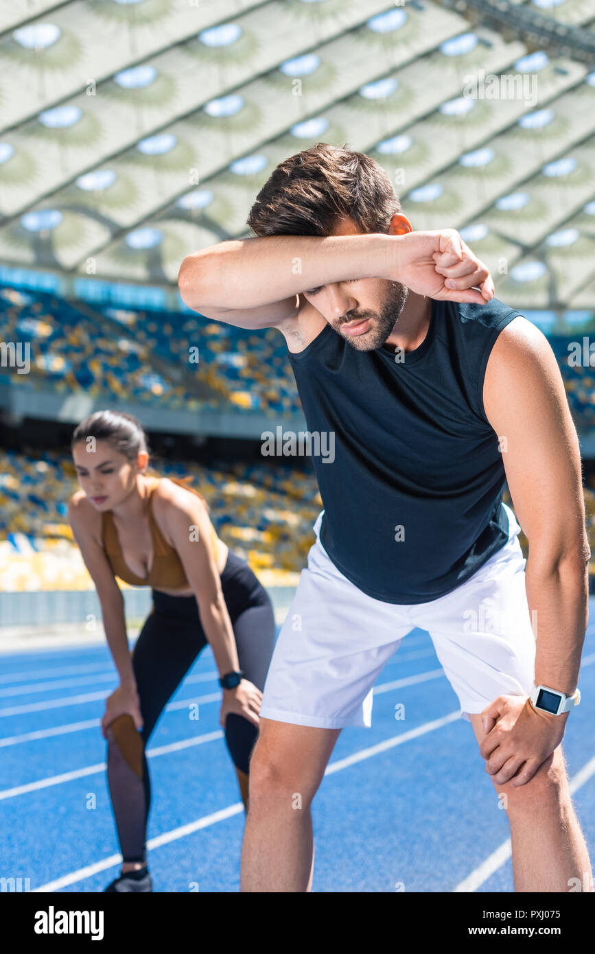 young exhausted couple standing on running track at sports stadium ...