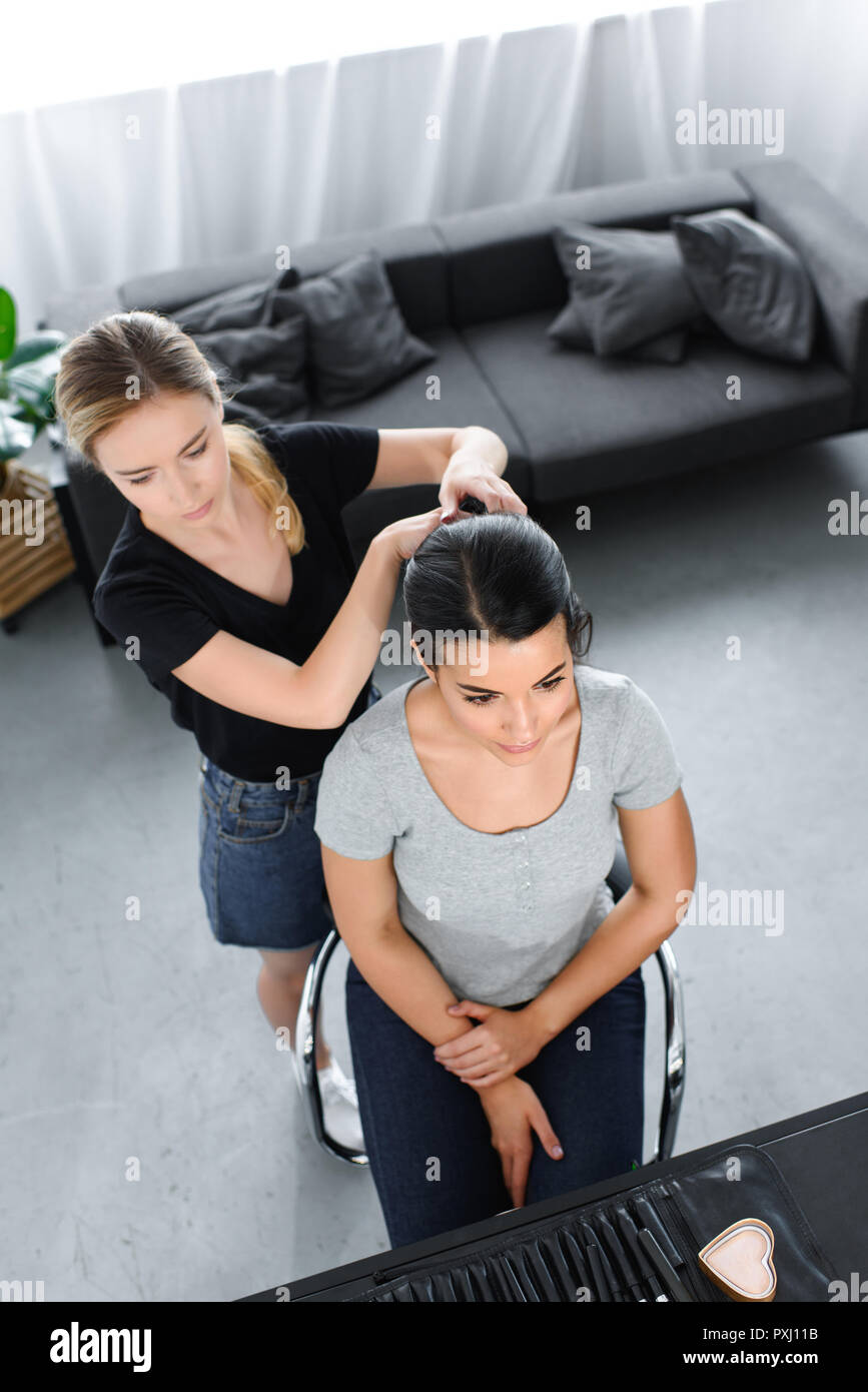 overhead view of hairstylist doing hairstyle to young woman on chair ...