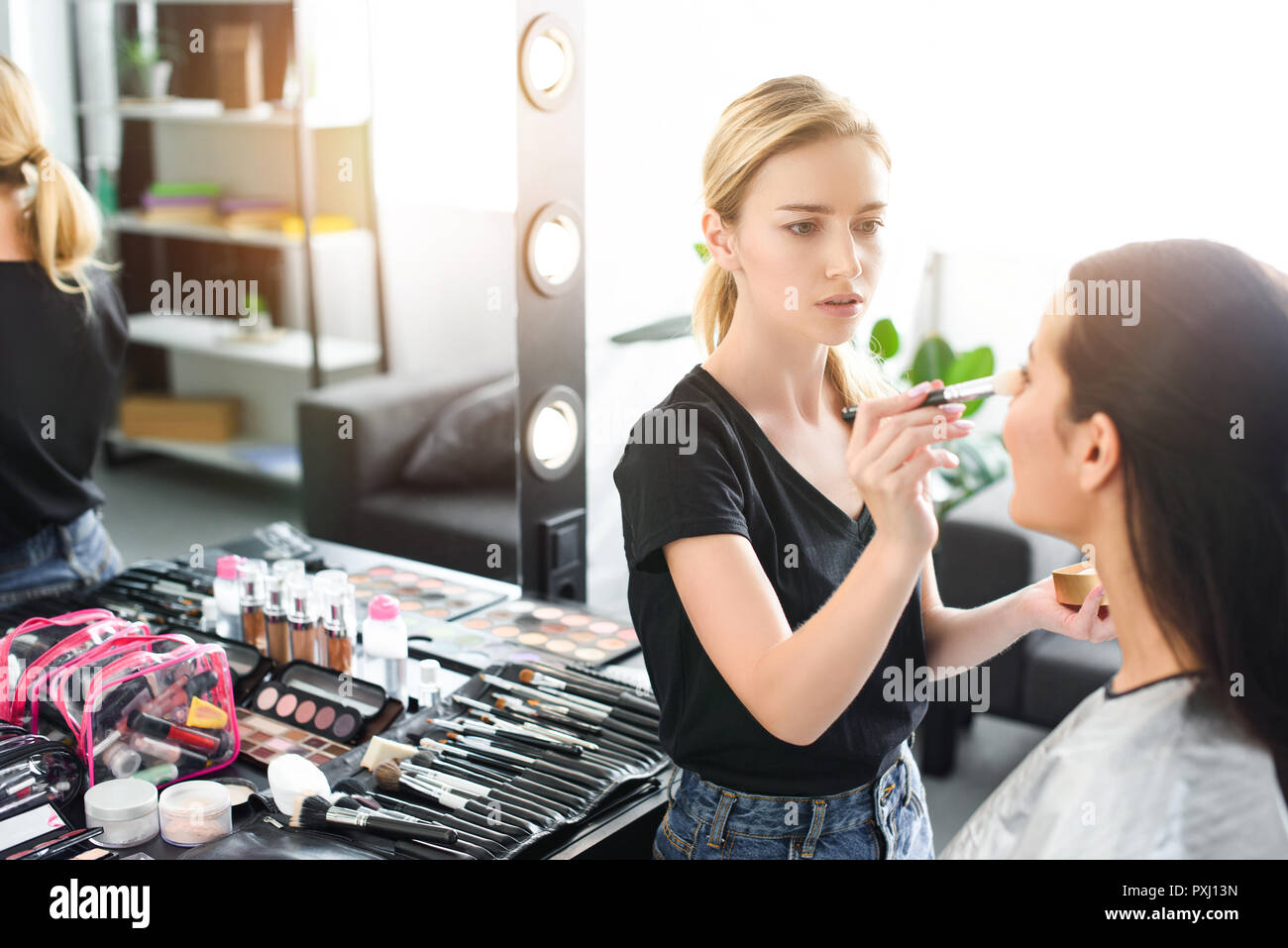 selective focus of beautiful young woman getting makeup done by makeup ...