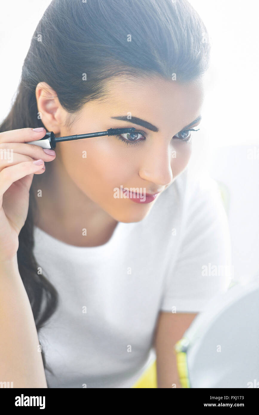 portrait of attractive young woman applying black mascara on eyelashes ...