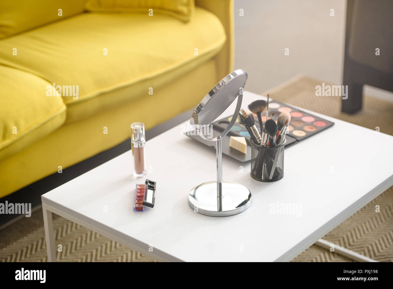 close up view of yellow sofa, mirror, makeup brushes and cosmetics on ...