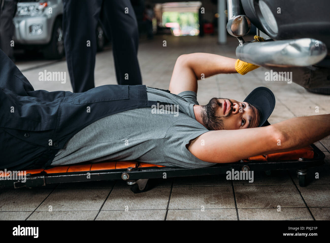 worker lying and working under car in mechanic shop Stock Photo - Alamy